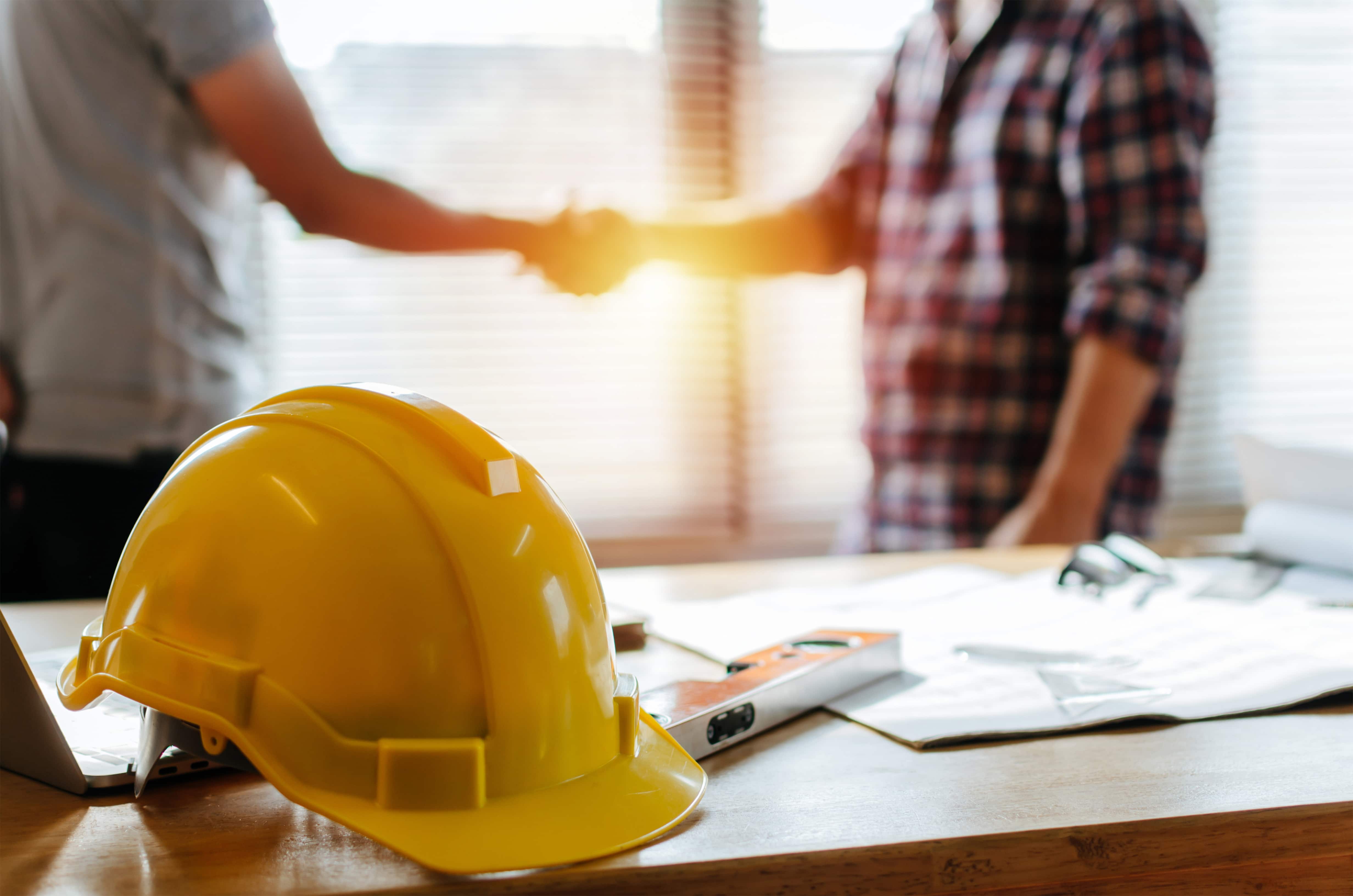 Two people shaking hands in the background with a yellow hard hat on a ...